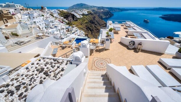 Terraço no telhado com edifícios brancos, piscina e vista para o mar e uma ilha ao longe.