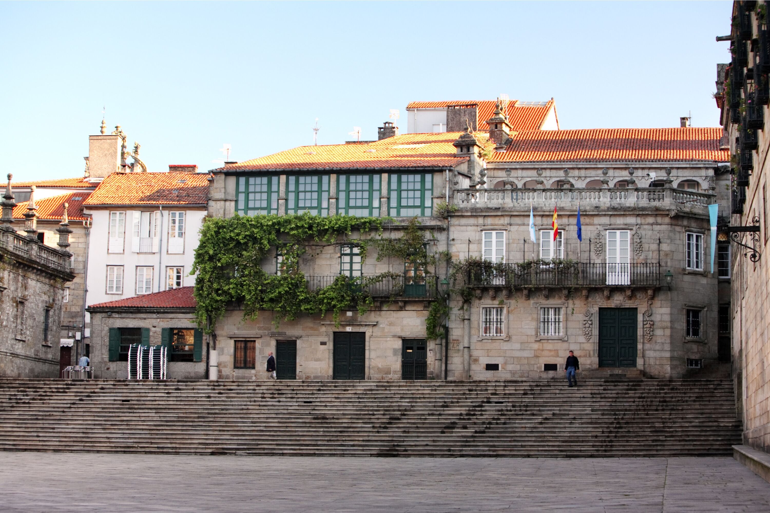 Um edifício histórico com fachada de pedra, persianas verdes e telhado de telhas vermelhas.