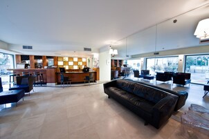 Um hall amplo com sofá de couro, vários espaços para sentar, balcão de recepção e grandes janelas com vista.
