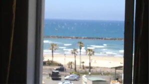 Vista do oceano por uma janela, com uma praia e palmeiras em primeiro plano.
