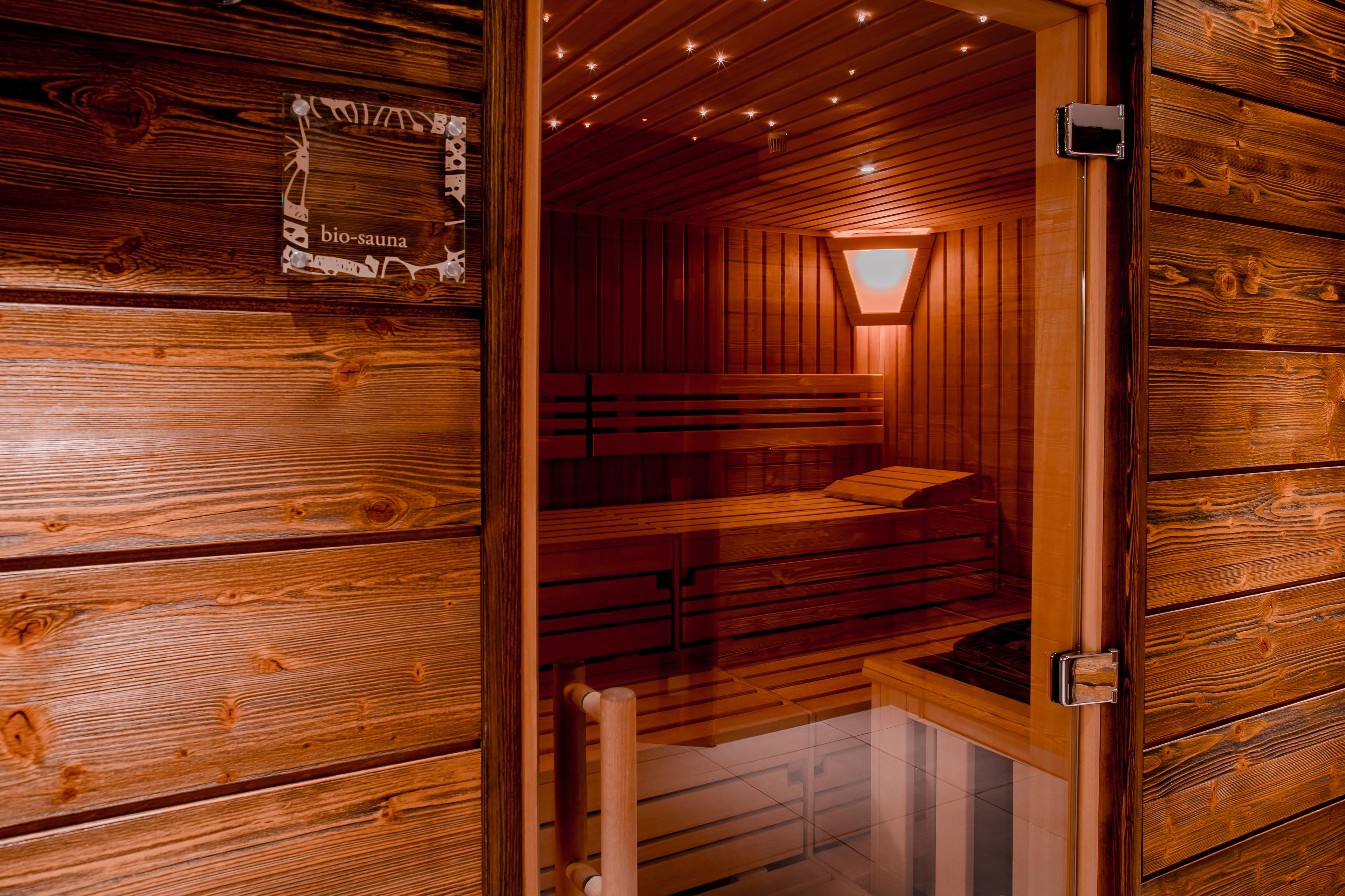 Uma sauna de madeira com um banco e uma pequena mesa, uma luminária na parede e uma porta de madeira.