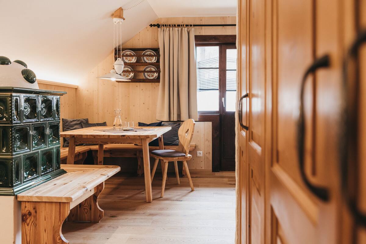 Um interior de madeira com uma mesa de jantar, cadeiras e um banco. Há um armário com pratos decorativos e um candeeiro pendente.
