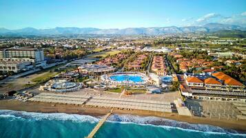 Vista aérea de um resort à beira-mar, com praia, piscina e um píer.