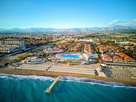 Vista aérea de um resort à beira-mar, com praia, piscina e um píer.