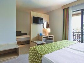 Quarto de hotel com cama, escrivaninha com cadeira, televisão na parede e varanda com vista.