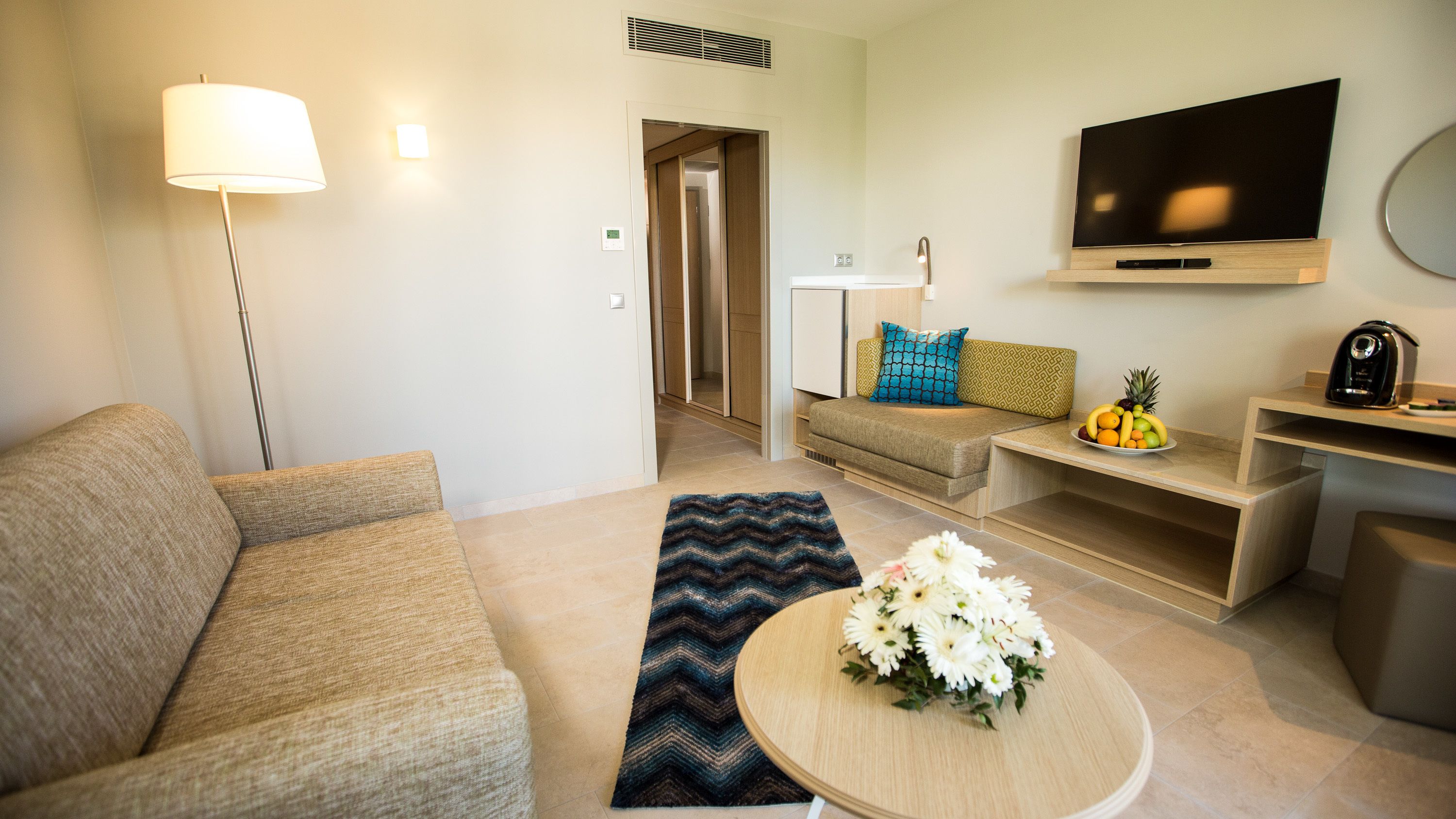 Uma sala de estar moderna com um sofá, uma mesa de centro com flores, uma TV de tela plana e uma fruteira.