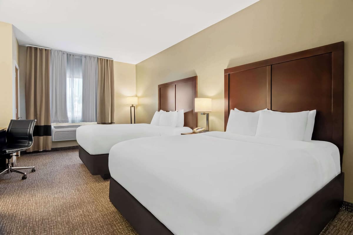 Quarto de hotel com duas camas, uma mesa e uma cadeira.