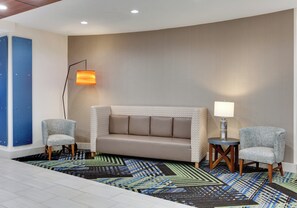 Quarto de hotel com sofá, duas poltronas, tapete estampado e luminária fixa na parede.
