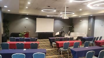 Uma sala de conferências com mesas, cadeiras, um pódio, uma tela de projetor e um carrinho de golfe.