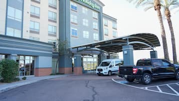Um hotel Holiday Inn com entrada coberta, estacionamento e uma palmeira ao fundo.