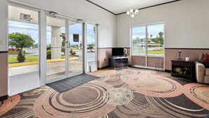 Um saguão de hotel com uma grande porta de entrada em vidro, uma televisão, um sofá e um candelabro.