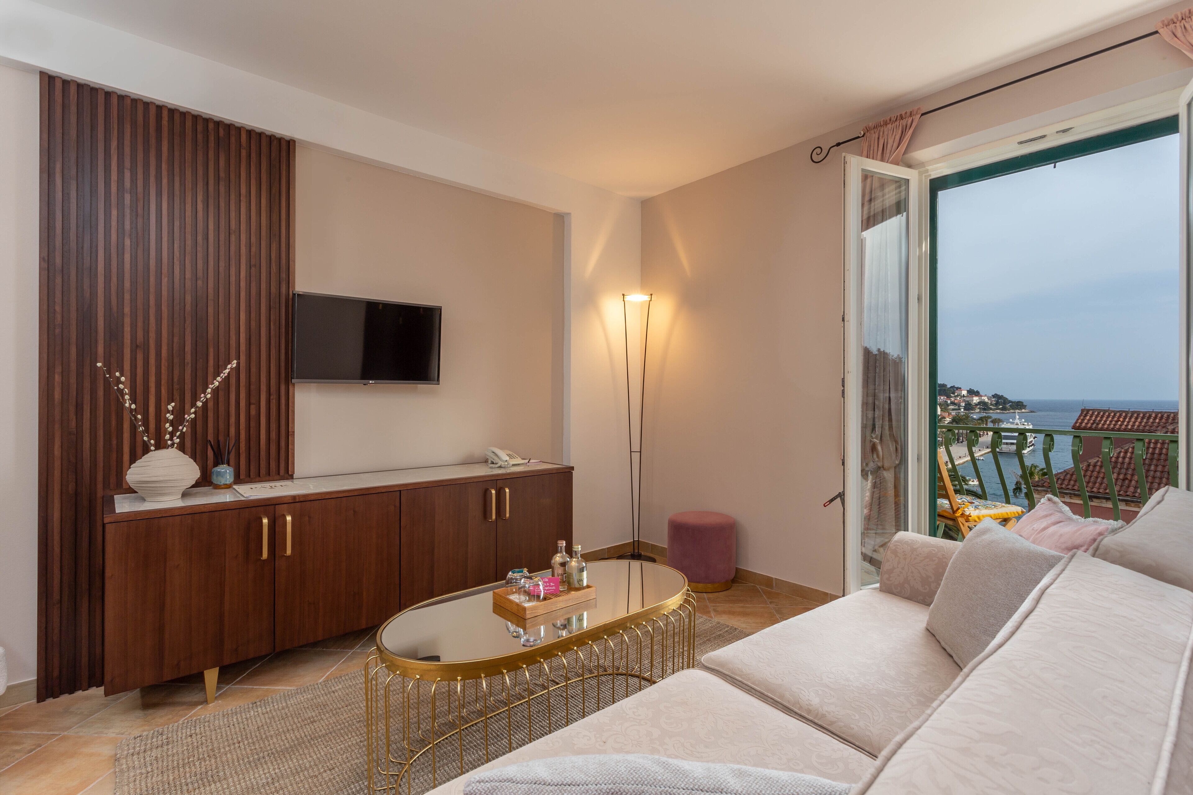 Uma sala de estar moderna com sofá, mesa de centro de vidro, armário de madeira, televisão de tela plana e uma varanda com vista para o mar.