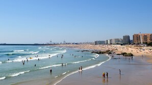 Praia cheia com ondas, pessoas e edifícios ao fundo.