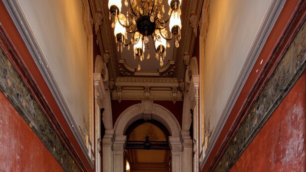 Uma escadaria imponente com corrimãos ricamente decorados e um lustre.