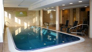 Piscina interior com chão de azulejos, um aviso acima e área de estar com cadeiras e uma mesa.
