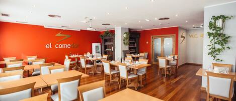 Um restaurante com várias mesas e cadeiras, uma parede vermelha com o logotipo 'el come dor', e um chão de madeira.