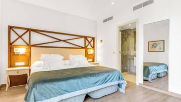 Quarto de hotel moderno com uma cama grande, cabeceira de madeira, luminárias de cabeceira e um banheiro visível por uma porta aberta.