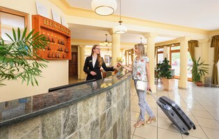 Uma área de recepção de hotel com balcão de mármore, mesa de atendimento e sistema de sinetas na parede.