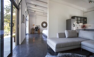 Uma sala de estar moderna com um sofá cinzento, uma máquina de café e uma área de cozinha com armários.