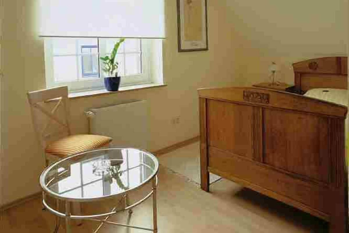 Um quarto com janela, radiador, armário de madeira, cadeira e mesa.