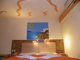 Quarto de hotel com cama, pintura de uma paisagem costeira e cabeceira de madeira.