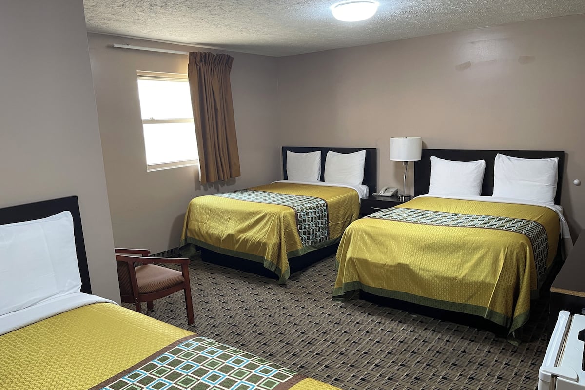 Quarto de hotel com duas camas, uma cadeira, uma escrivaninha e uma luminária.