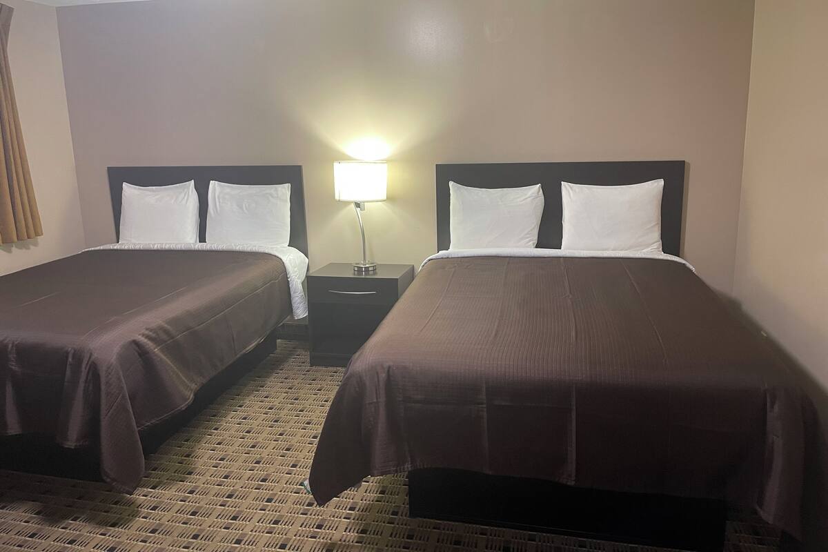 Quarto de hotel com duas camas, cada uma com cabeceira, mesa de cabeceira e abajur, além de um carpete estampado.