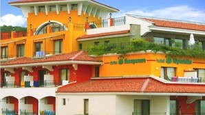 Um hotel com fachada amarelo vibrante, várias varandas e telhado de telhas vermelhas.
