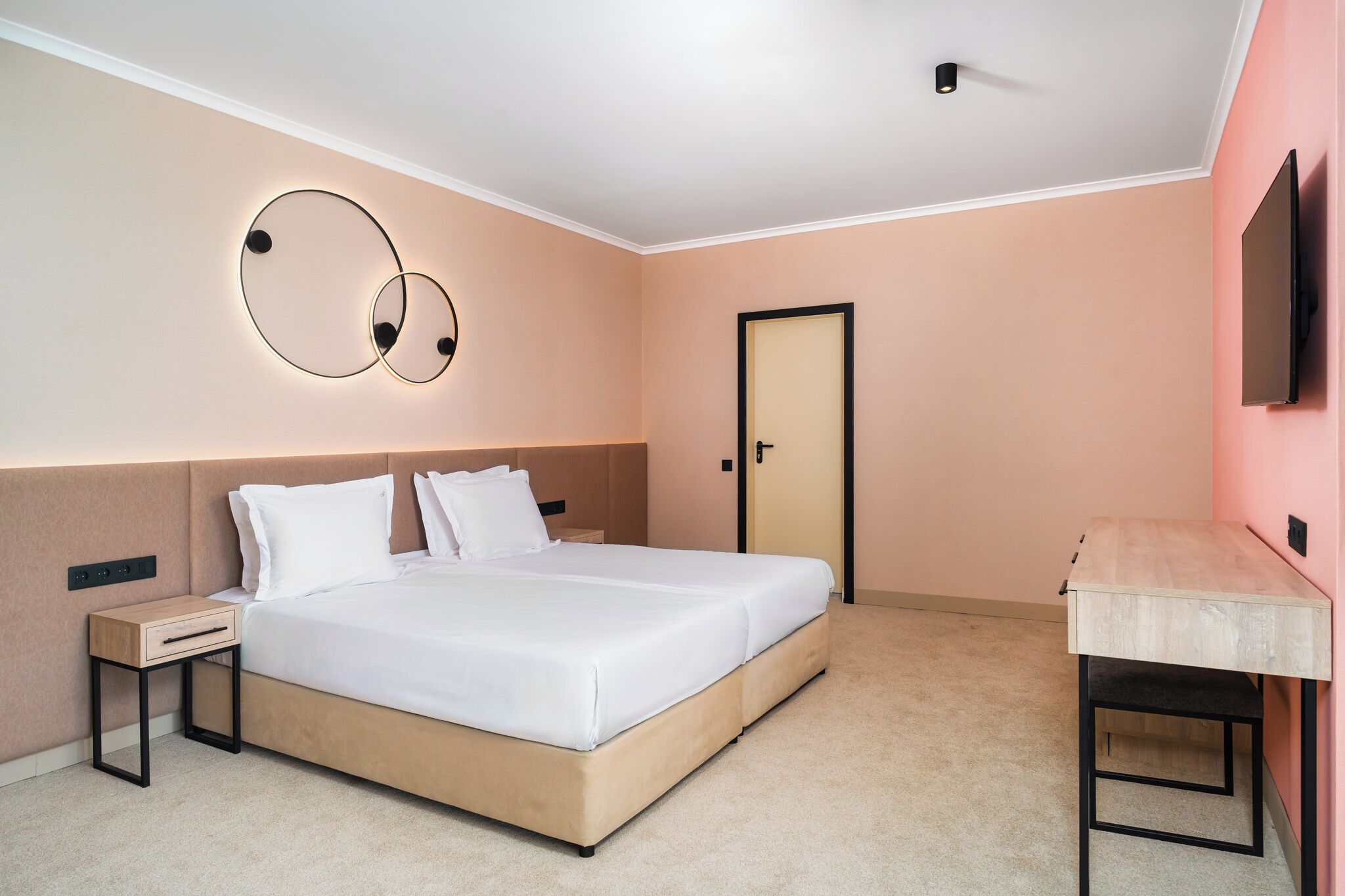 Quarto com cama, mesa de cabeceira, luminária na parede e televisão.