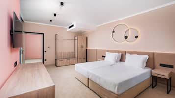 Quarto de hotel moderno com uma cama grande, uma mesinha de cabeceira de madeira, uma TV de tela plana na parede e um lustre no teto.