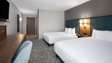Quarto de hotel com duas camas, uma escrivaninha, uma televisão e uma porta.