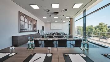 Uma sala de conferências com uma mesa grande, cadeiras, tela de projetor e vista para o exterior.