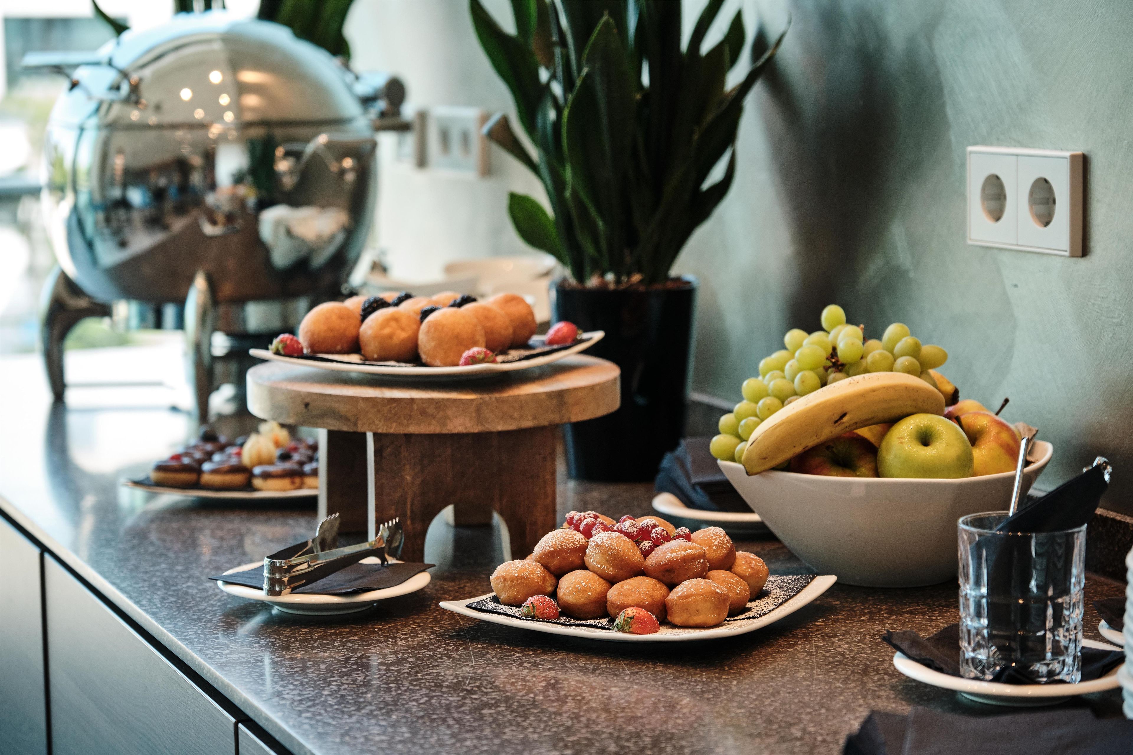 Mesa de buffet com diversos alimentos, incluindo doces, frutas e uma tigela de uvas.