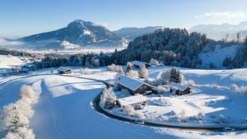 Paisagem coberta de neve com uma estrada sinuosa, vários edifícios e uma montanha ao fundo.