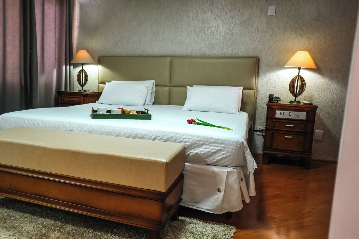 Quarto de hotel com uma cama, mesas de cabeceira, luminária e uma mesinha com bandeja.