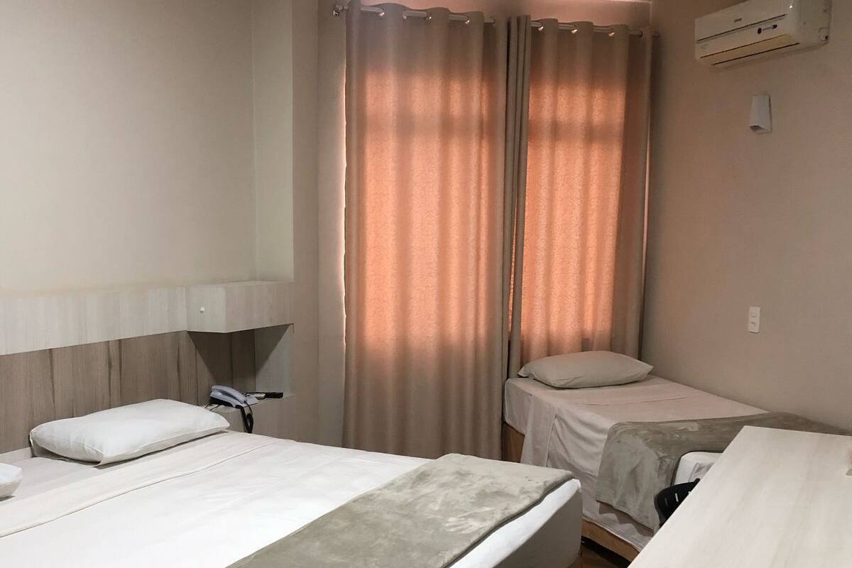 Quarto com duas camas, uma escrivaninha, uma cadeira e uma janela com cortinas.