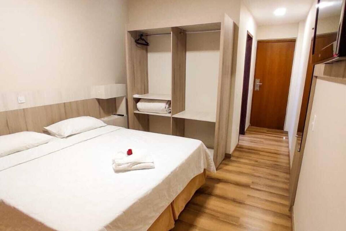 Quarto de hotel com cama, guarda-roupa e chão de madeira.