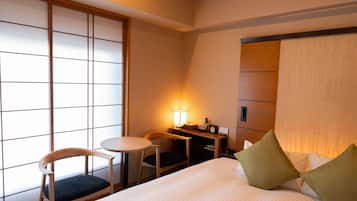 Quarto de hotel com uma cama, uma mesa com luminária, uma cadeira e vista através de um ecrã shoji.