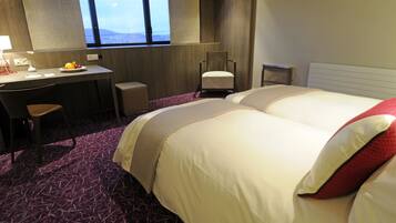 Quarto de hotel com cama, escrivaninha, cadeira e janela com vista.