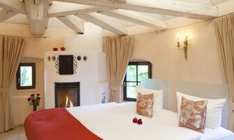 Quarto com lareira, cama com almofadas estampadas e janela com cortinas.