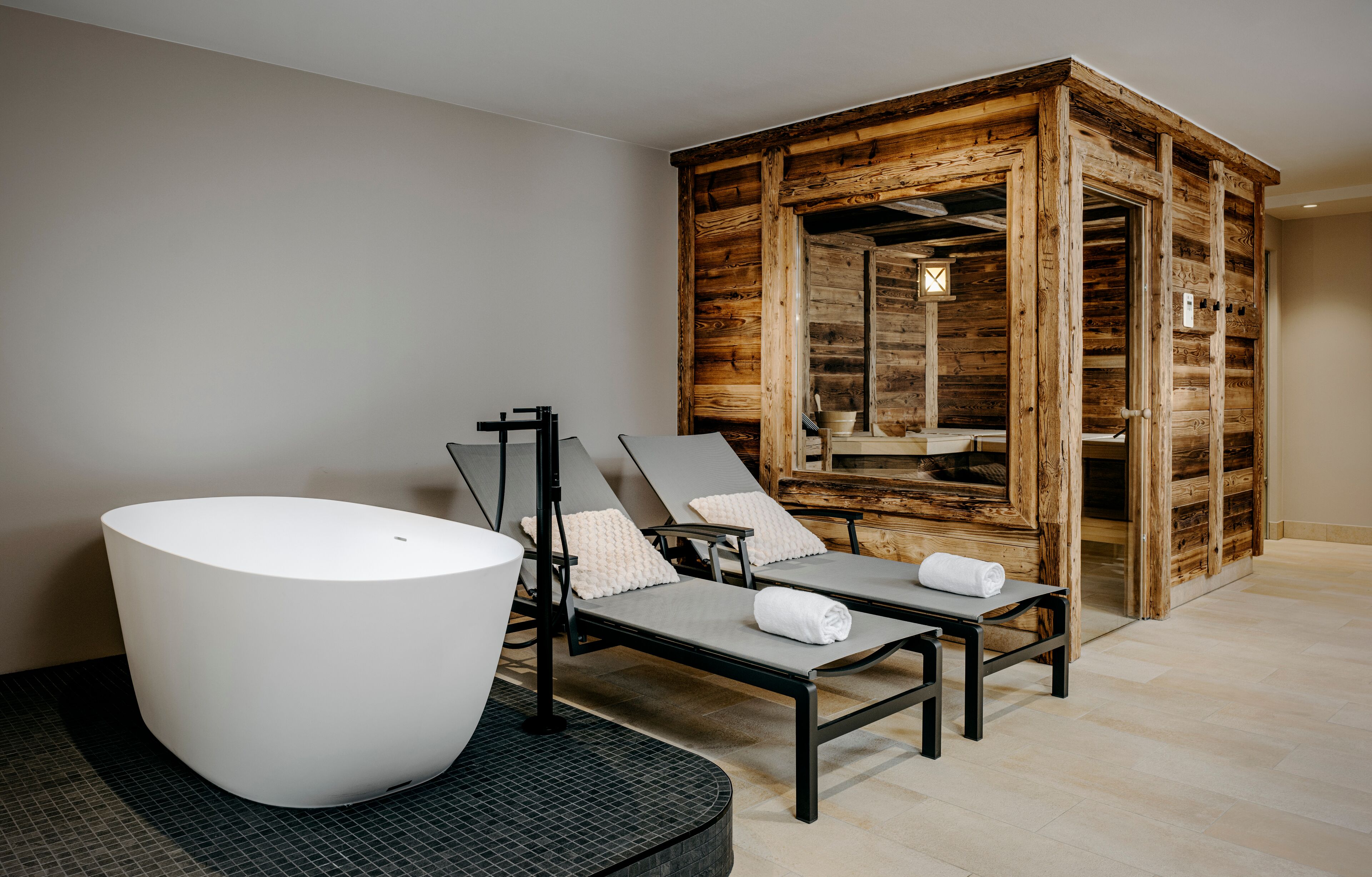 Um quarto de spa com uma banheira grande e branca, duas poltronas de descanso e uma estrutura de sauna de madeira.