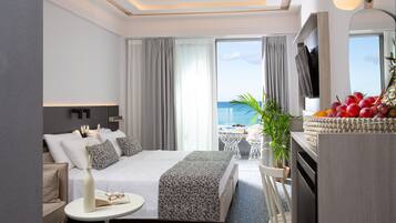 Quarto de hotel moderno com uma cama grande, uma mesa pequena com um vaso e um livro, uma televisão e uma varanda com vista para o mar.