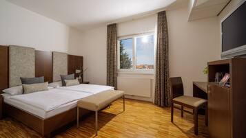 Quarto de hotel com uma cama grande, uma escrivaninha, uma cadeira e uma televisão.