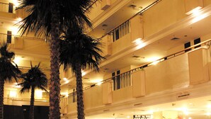Um átrio de hotel com vários andares, com um recurso central de água, palmeiras e diversas áreas de refeições.