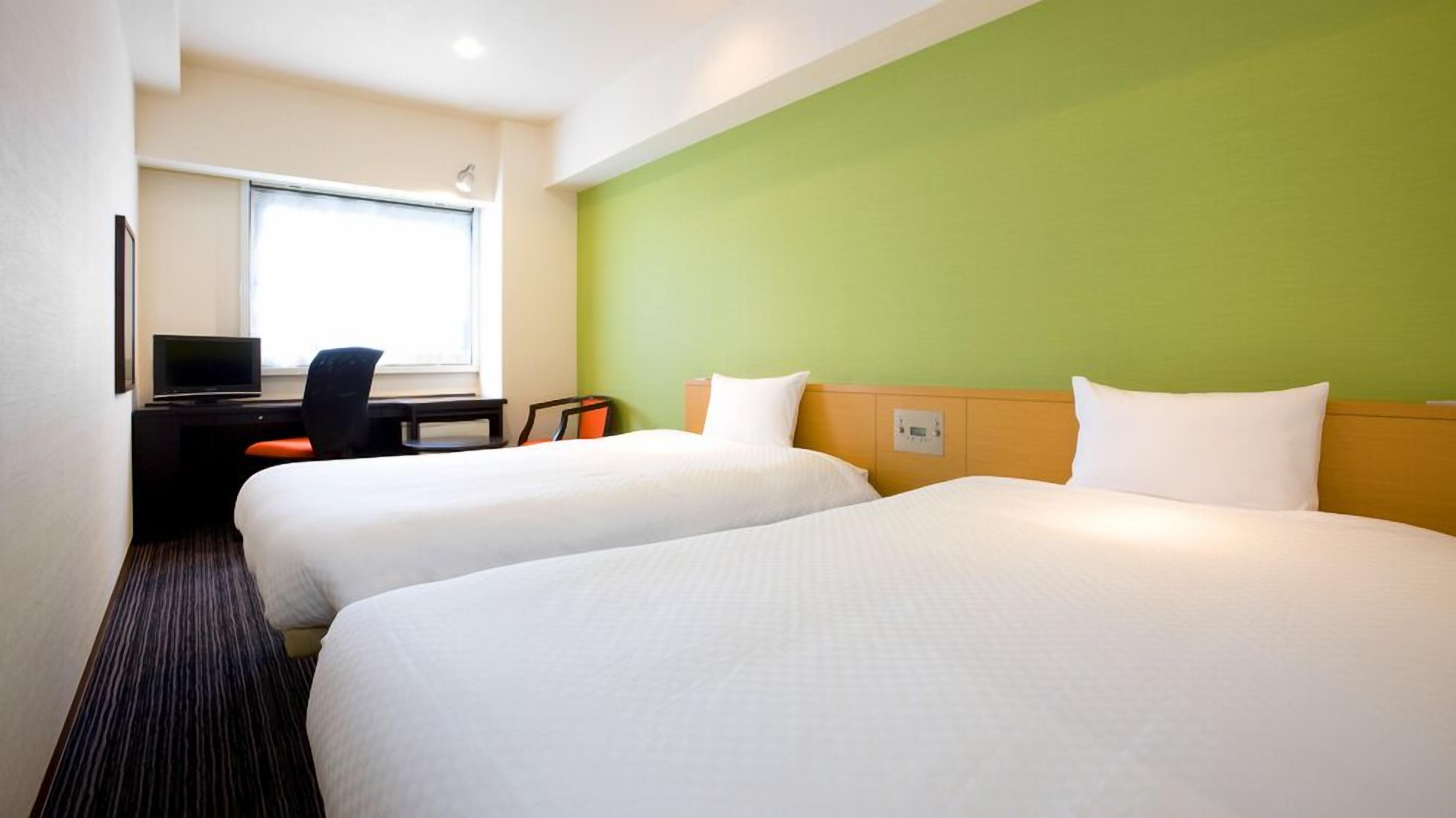 Quarto de hotel com duas camas, uma escrivaninha com cadeira, televisão e janela.