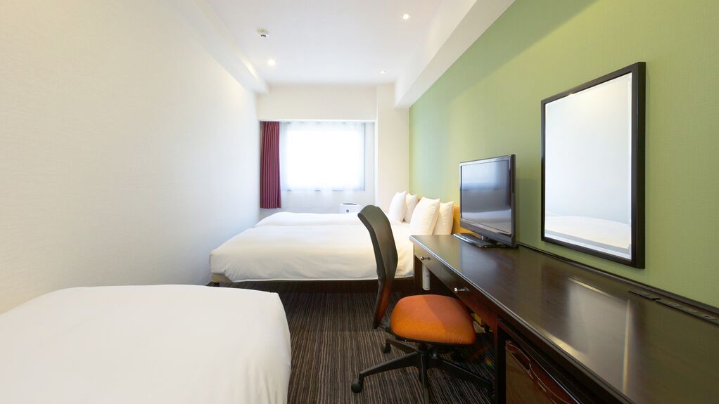 Quarto de hotel com duas camas, uma escrivaninha com televisão e uma janela grande com cortinas.