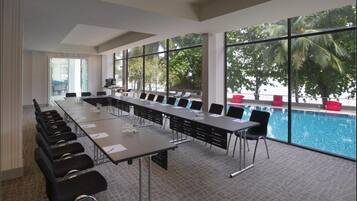 Uma sala de conferências com uma mesa comprida e cadeiras, janelas amplas com vista para uma piscina e palmeiras, e piso coberto de carpete.