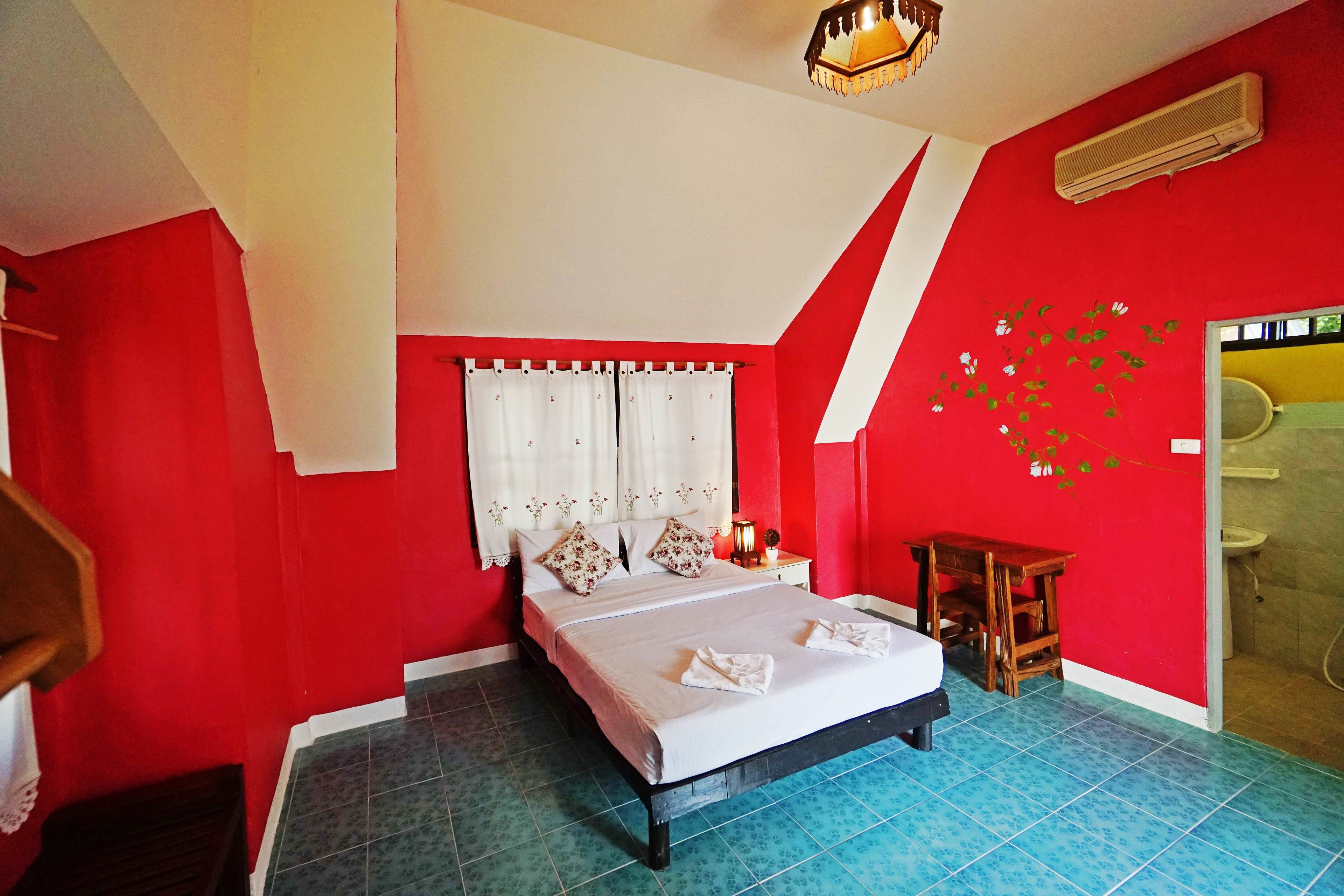 Quarto com cama, mesa de madeira pequena, mesa de cabeceira, espelho e banheiro com pia e vaso sanitário.