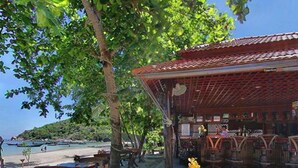 Um restaurante à beira-mar com mesas ao ar livre, área coberta e vista para a praia e o oceano.