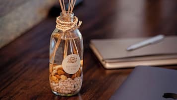 Uma garrafa de vidro com etiqueta, cheia de pequenos pedregulhos e raminhos, colocada sobre uma mesa de madeira ao lado de um laptop.